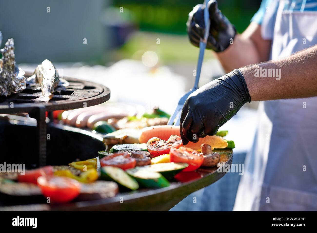 The cook prepares vegetables and meat on the grill in summer Stock ...
