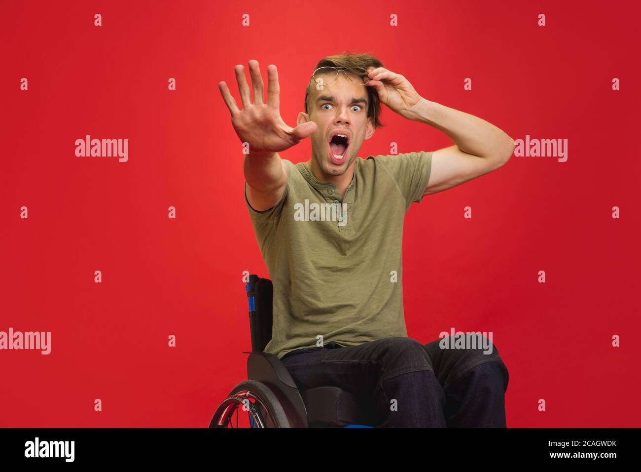 Scared, shocked. Caucasian young disabled man's portrait on red studio ...