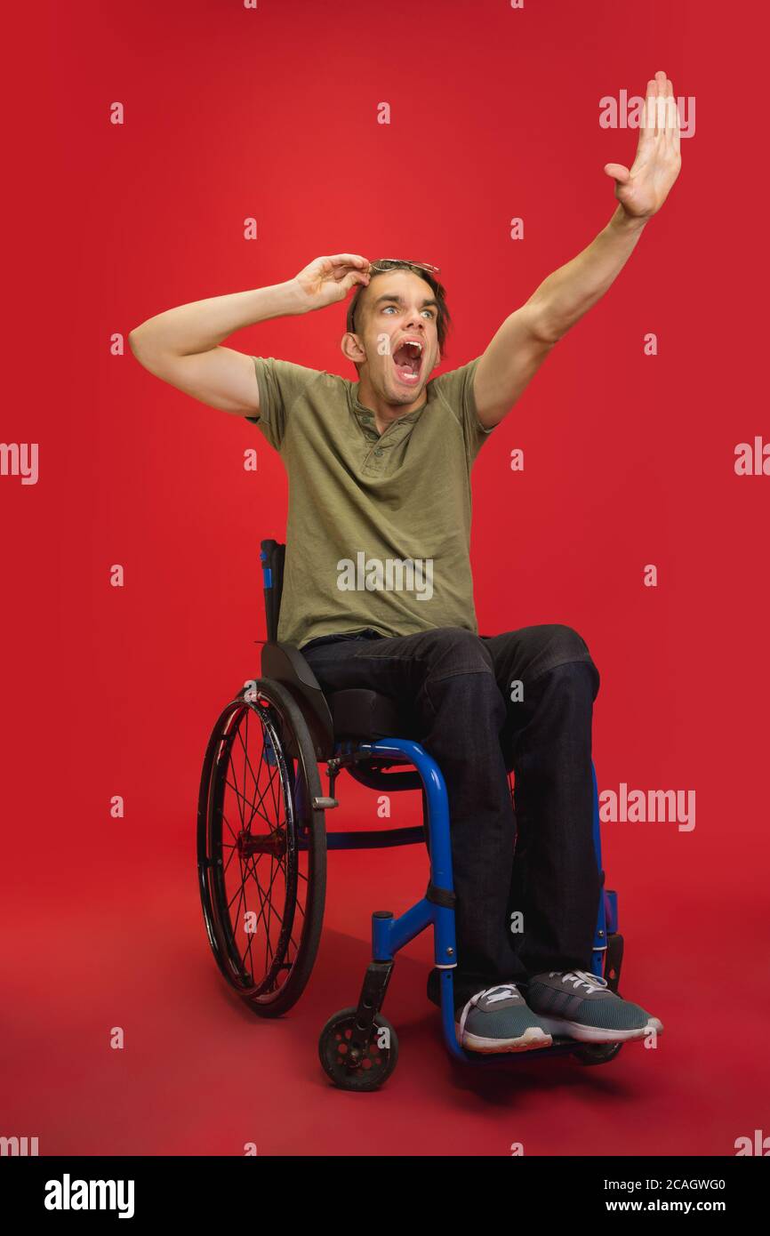 Scared, shocked. Caucasian young disabled man's portrait on red studio ...