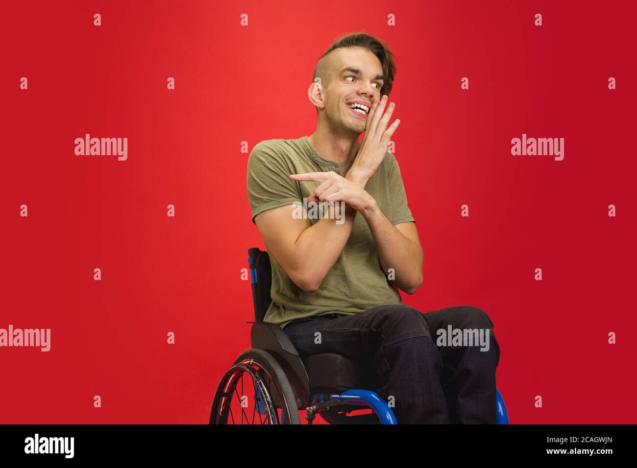 Gossip. Caucasian young disabled man's portrait isolated on red studio ...