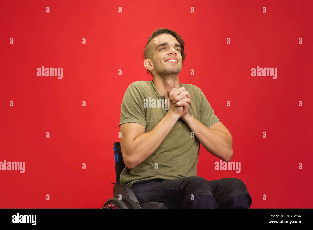 Hopeful praying. Caucasian young disabled man's portrait on red studio ...