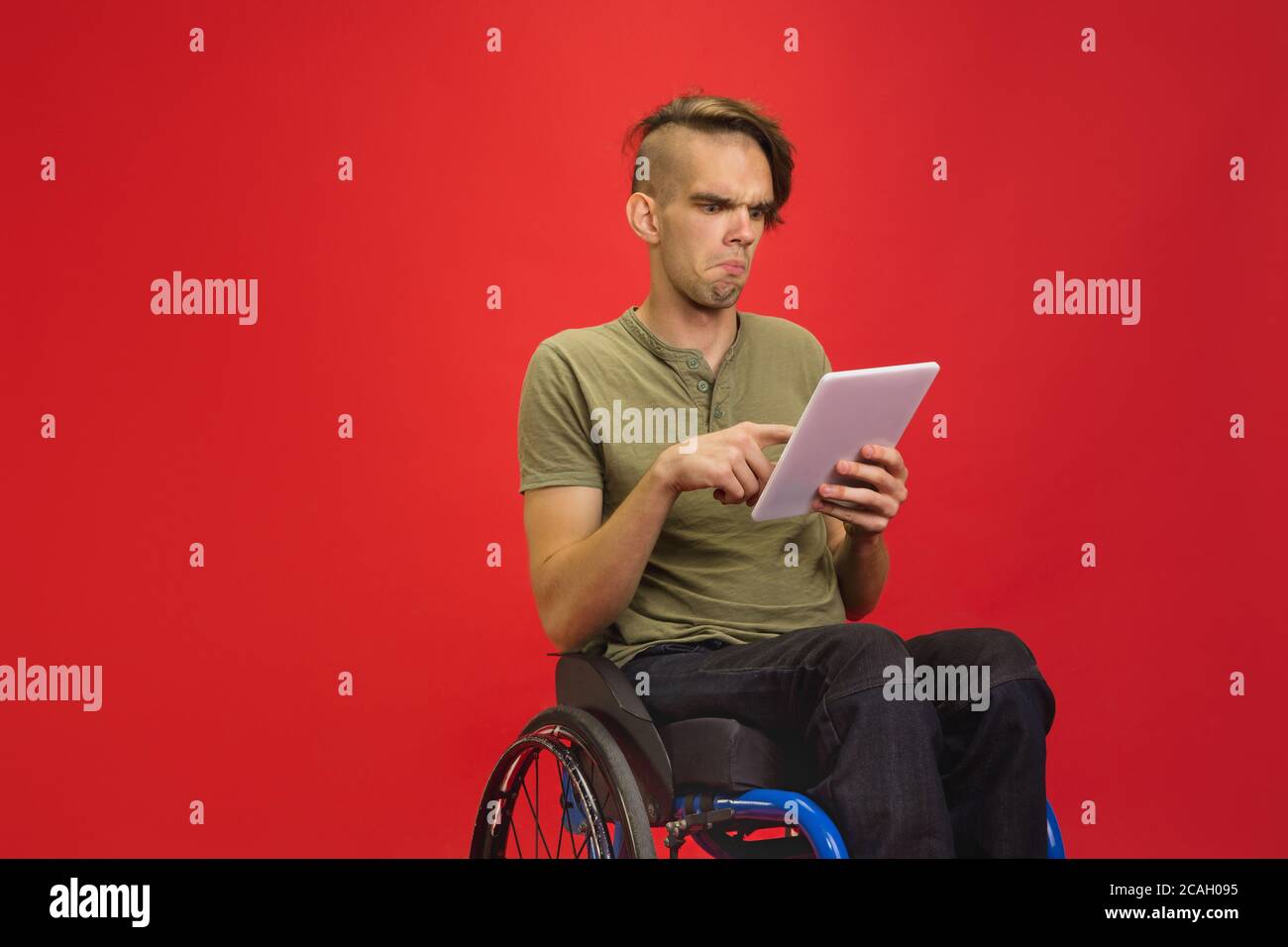 Scrolling tablet. Caucasian young disabled man's portrait on red studio ...