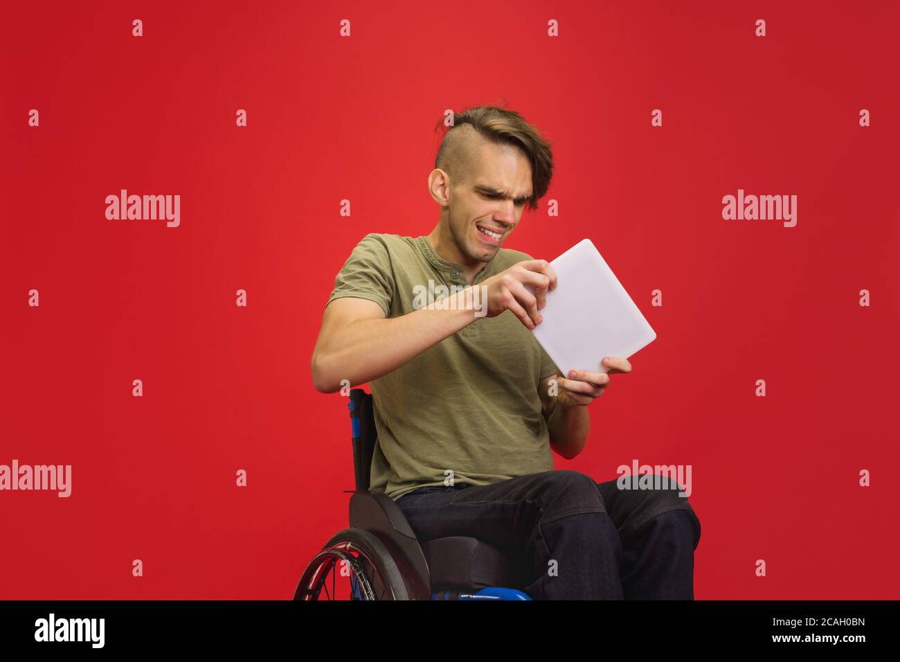 Playing tablet. Caucasian young disabled man's portrait on red studio ...