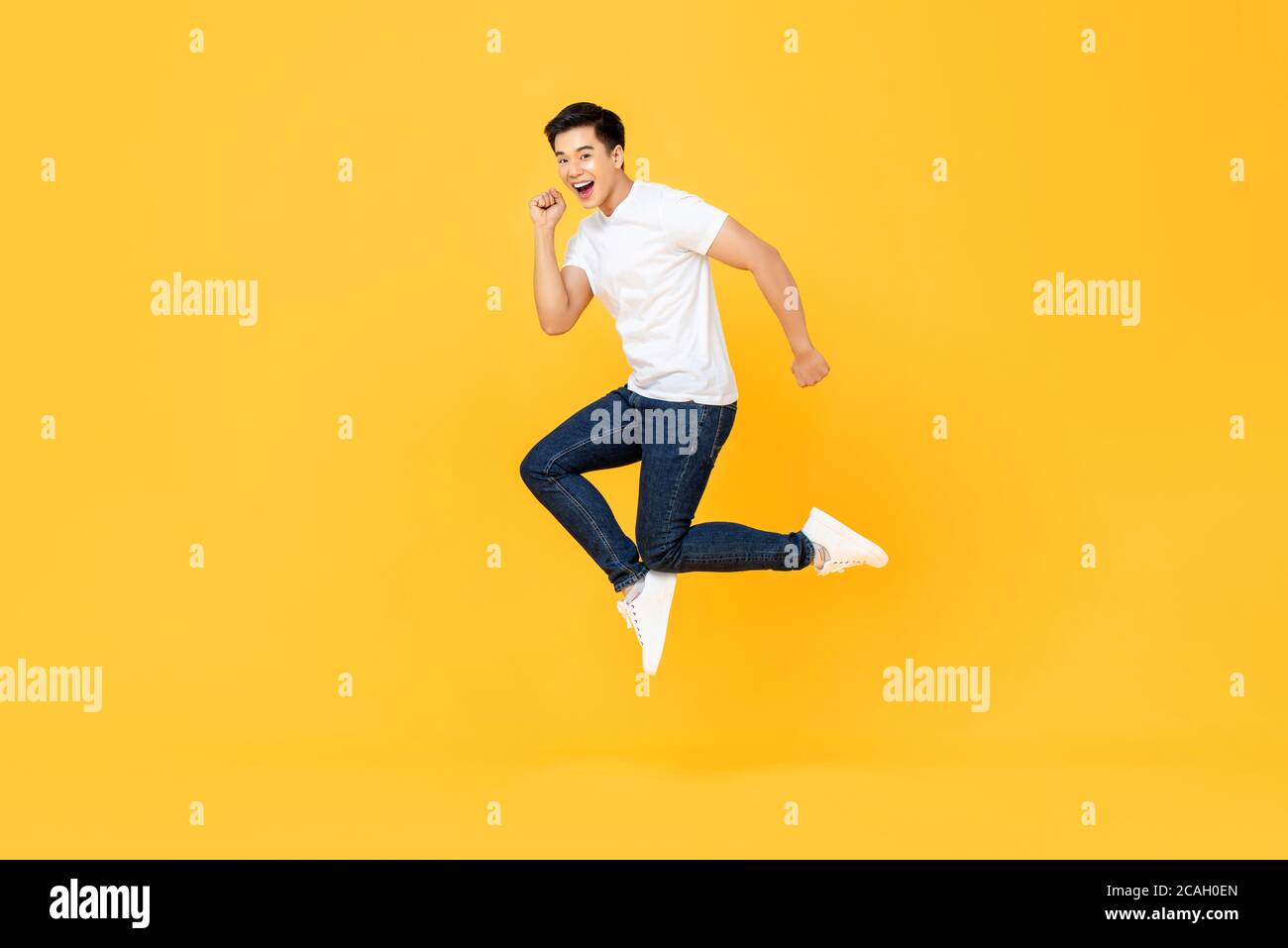 Happy excited young Asian man jumping isolated on yellow studio ...