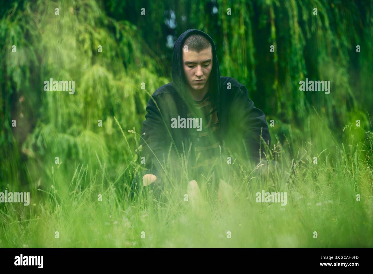 Portrait of a sad, crouching man in a black hoodie Stock Photo - Alamy