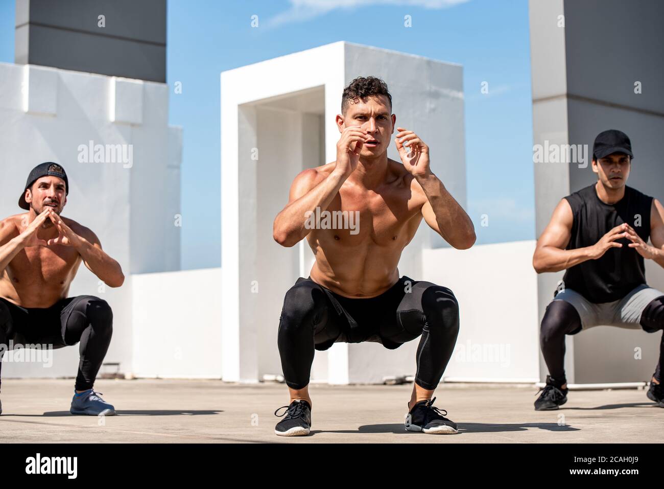 Group of fit sports men doing squat bodyweight workout training ...