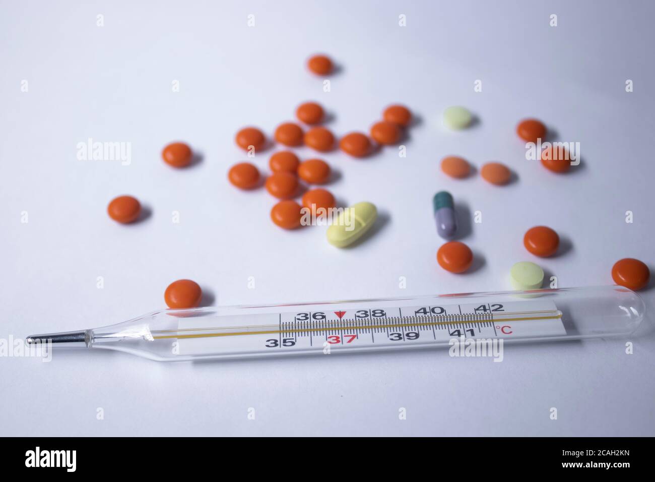mercury thermometer with a bunch of pills on a white background ...