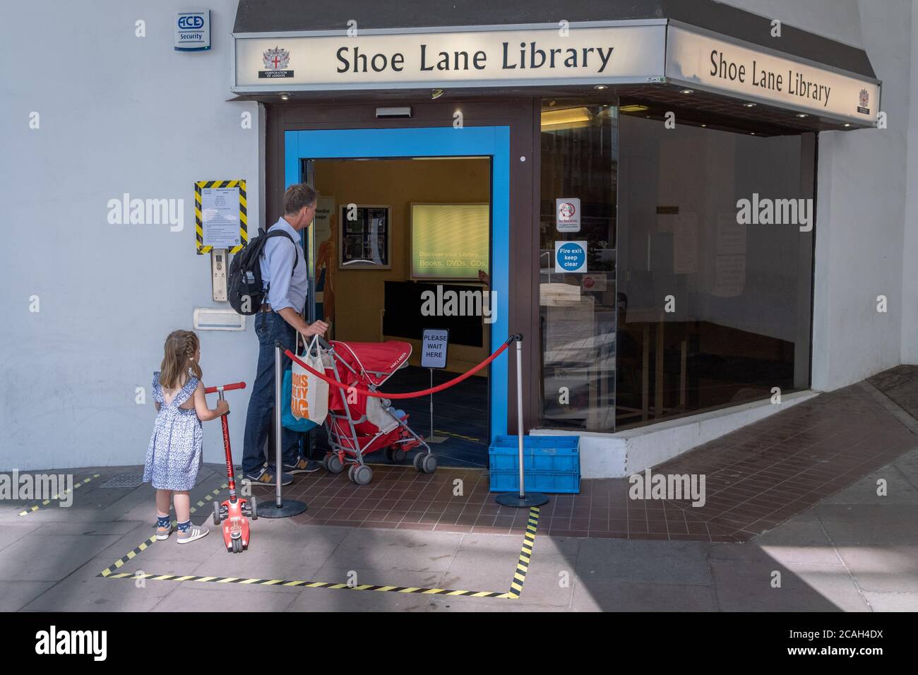 A father and his young children wait to safely enter Shoe Lane Library ...