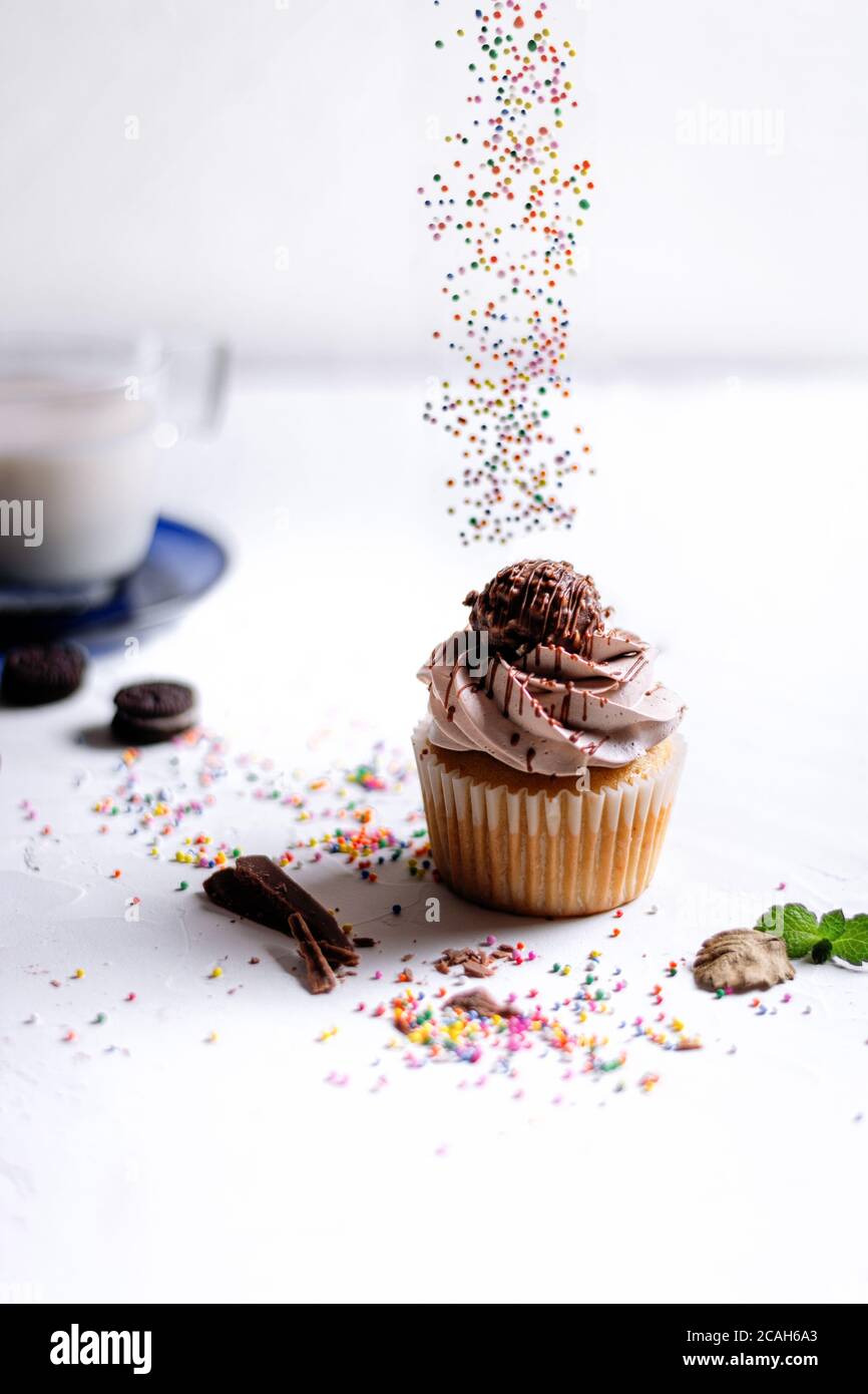 Vertical shot of a chocolate cupcake and sprinkles pouring from top ...