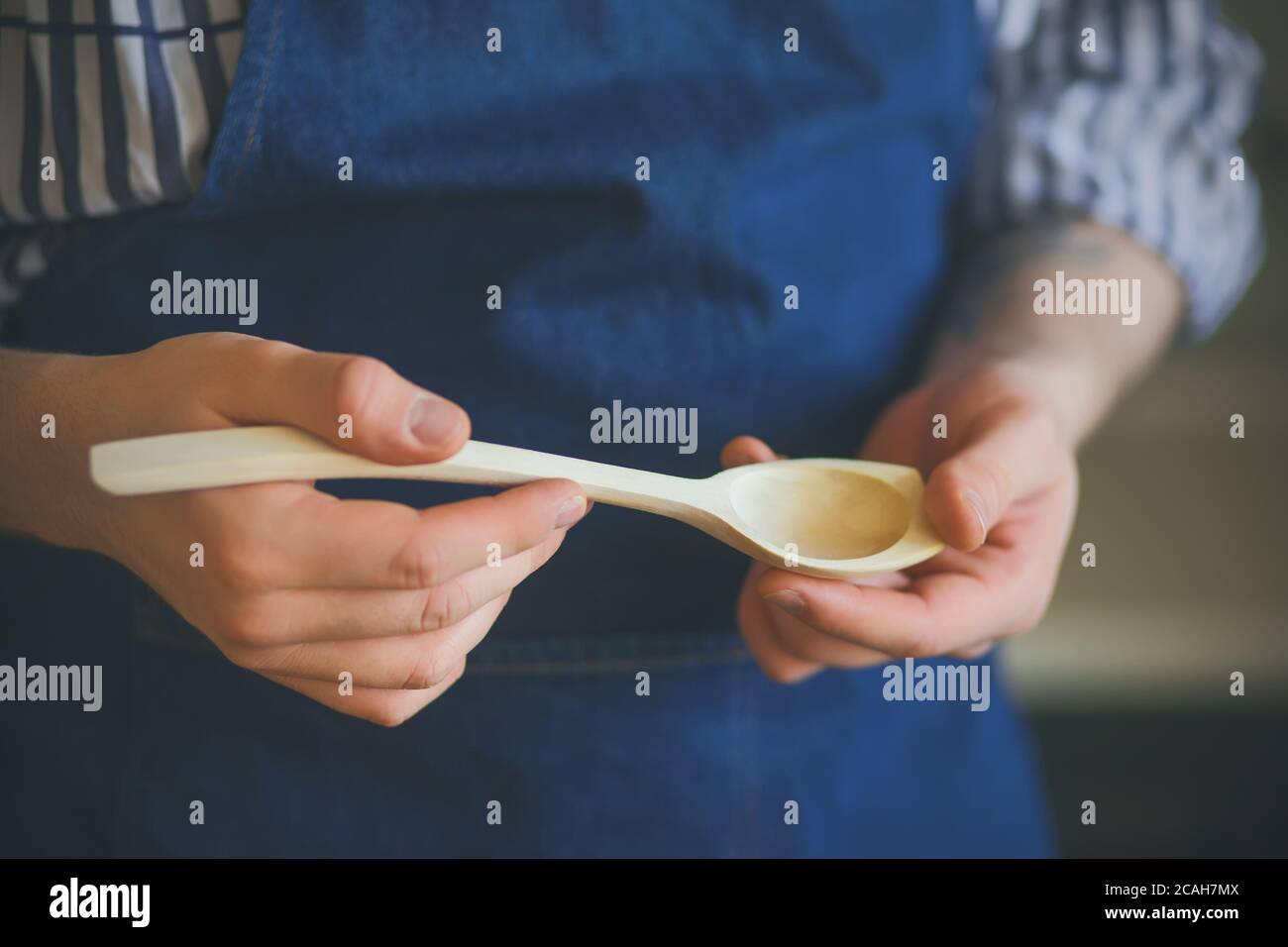A chef in a blue apron holds a wooden kitchen utensil - an elegant ...