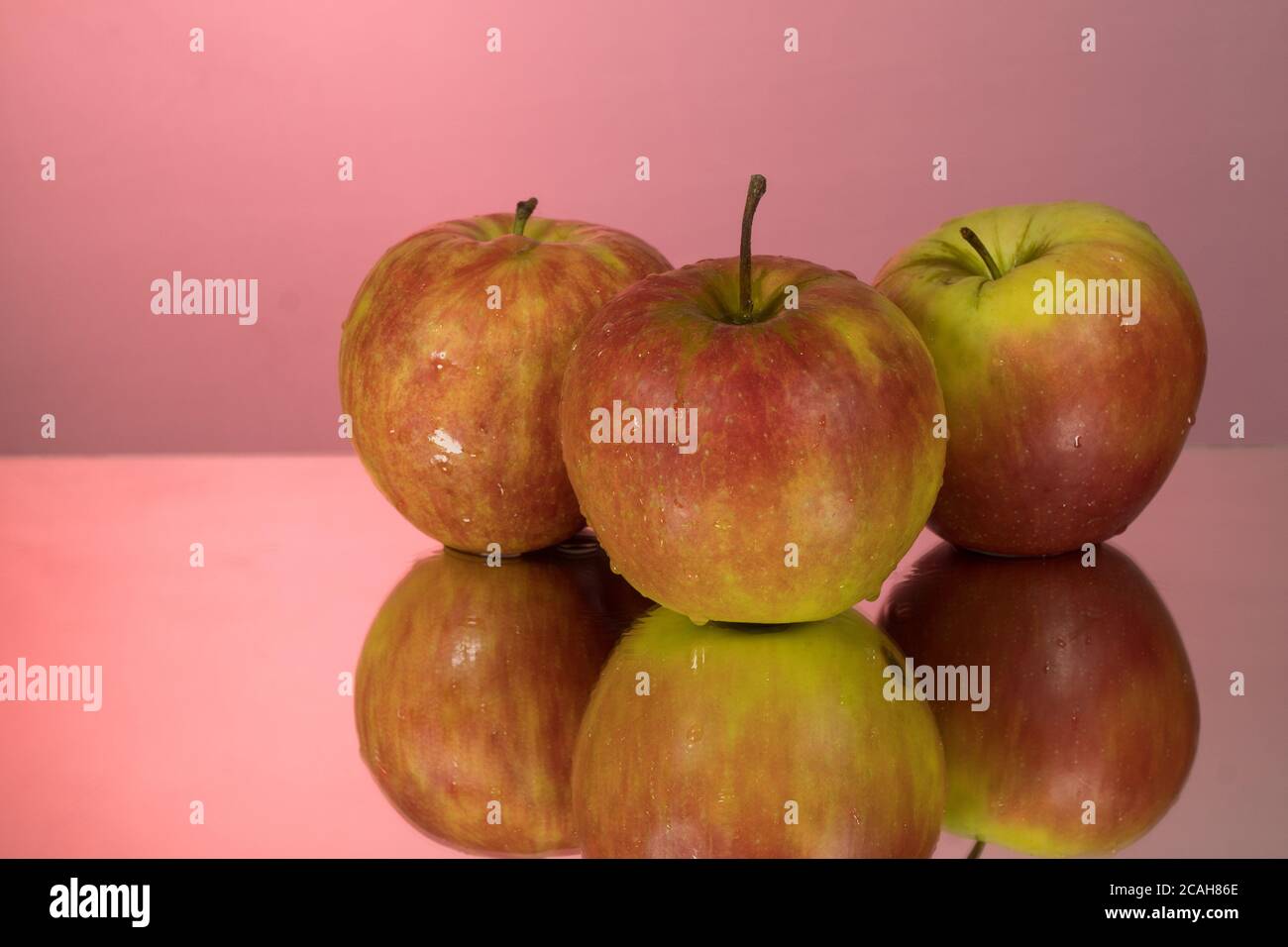 Three red apples on mirroring table on mirror red background with ...