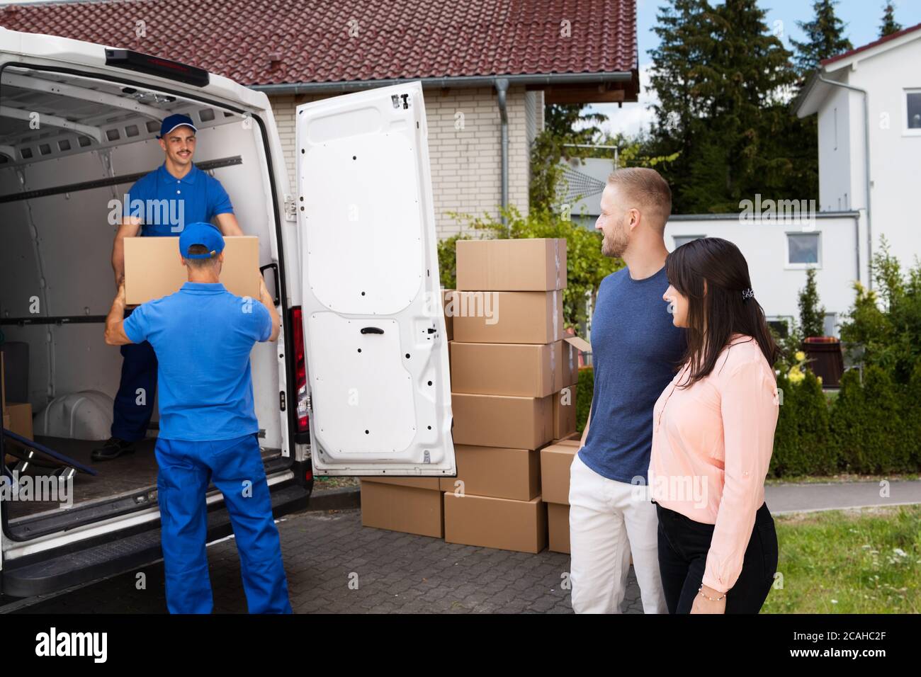 Happy Family Couple Watching Movers Unload Boxes From Truck Stock Photo ...