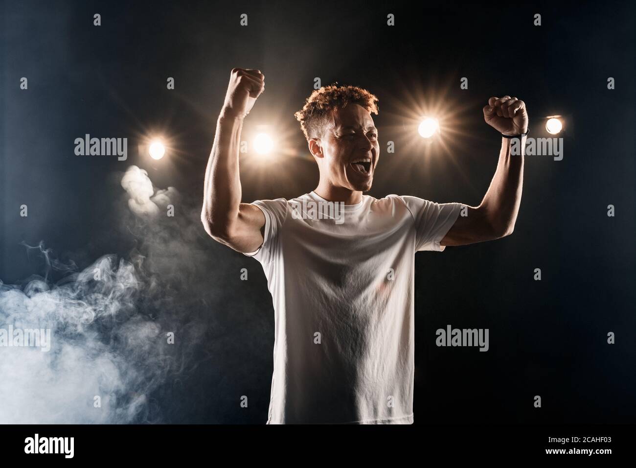 Football. Mulatto guy standing isolated on dark filed hands up shouting ...