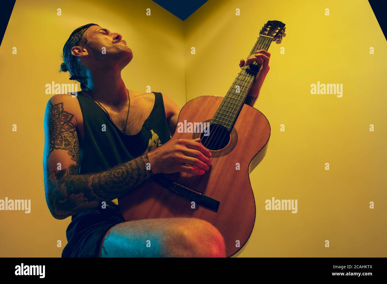Young musician with guitar performing on yellow background in neon ...