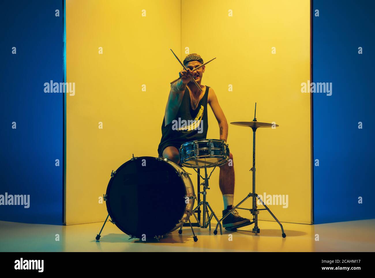 Rockstar. Young musician with drums performing on yellow background in ...