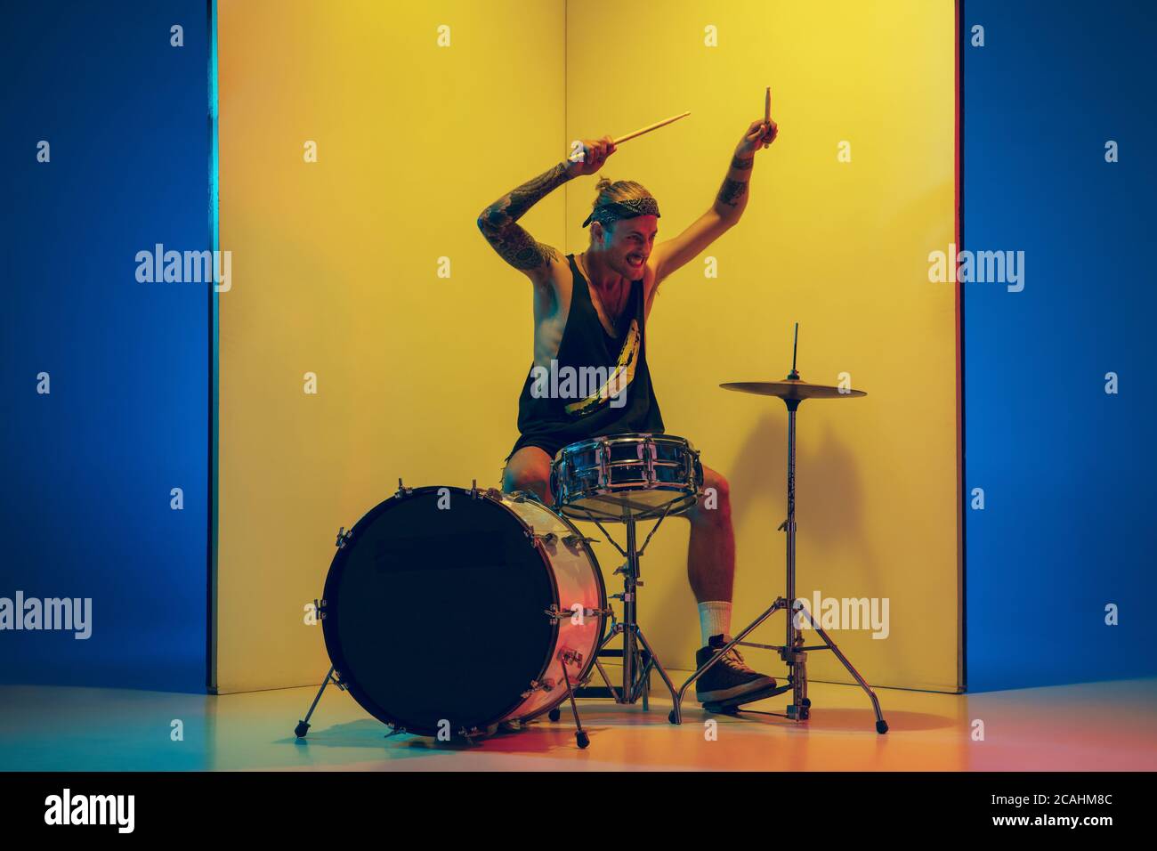 Youth. Young musician with drums performing on yellow background in ...