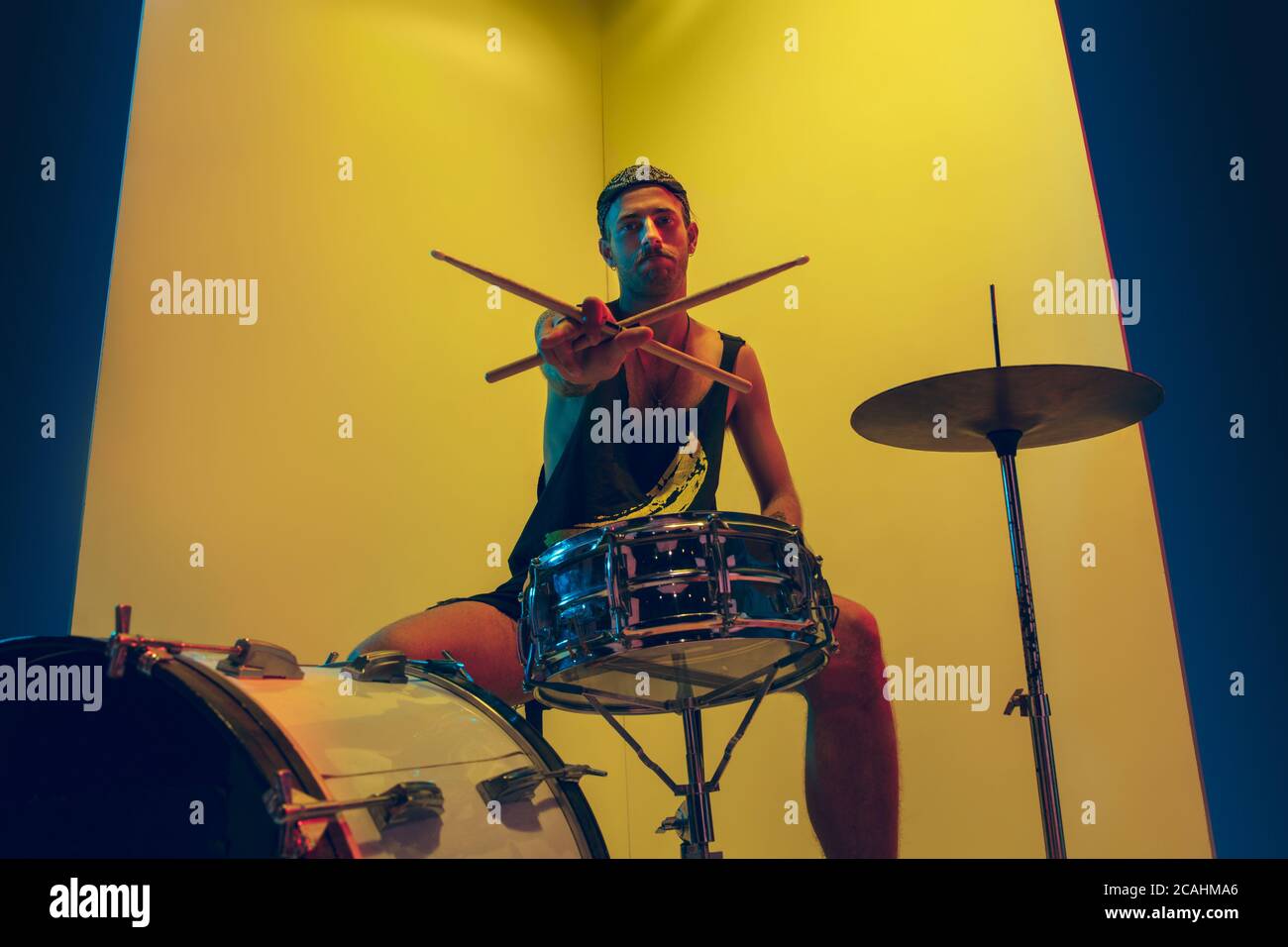 Youth. Young musician with drums performing on yellow background in ...