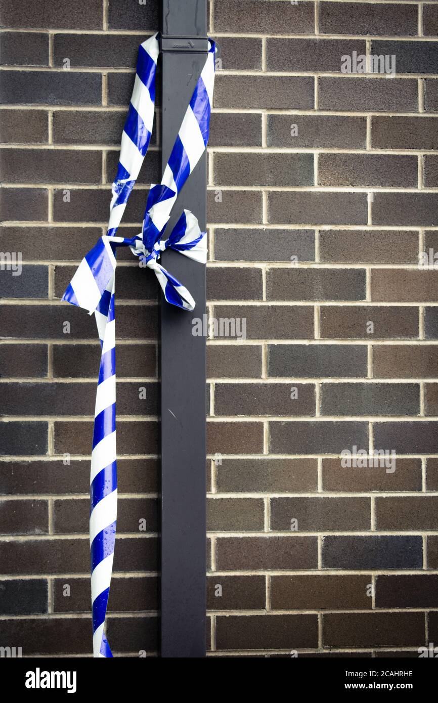 White and blue caution tape tied to a n iron post against a brick wall ...