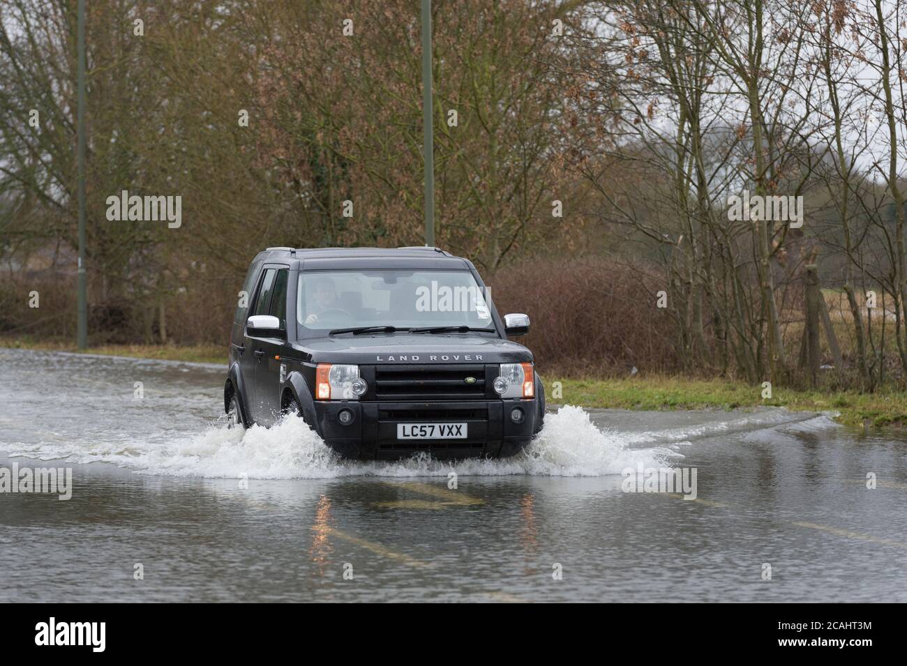 A car driving through flood waters on Chertsey Lane, Egham Hythe ...