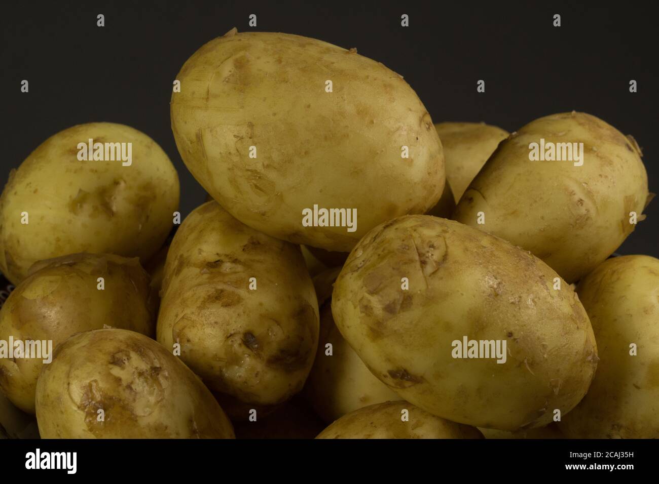 Raw fresh organic potatoes on black wooden table against dark ...