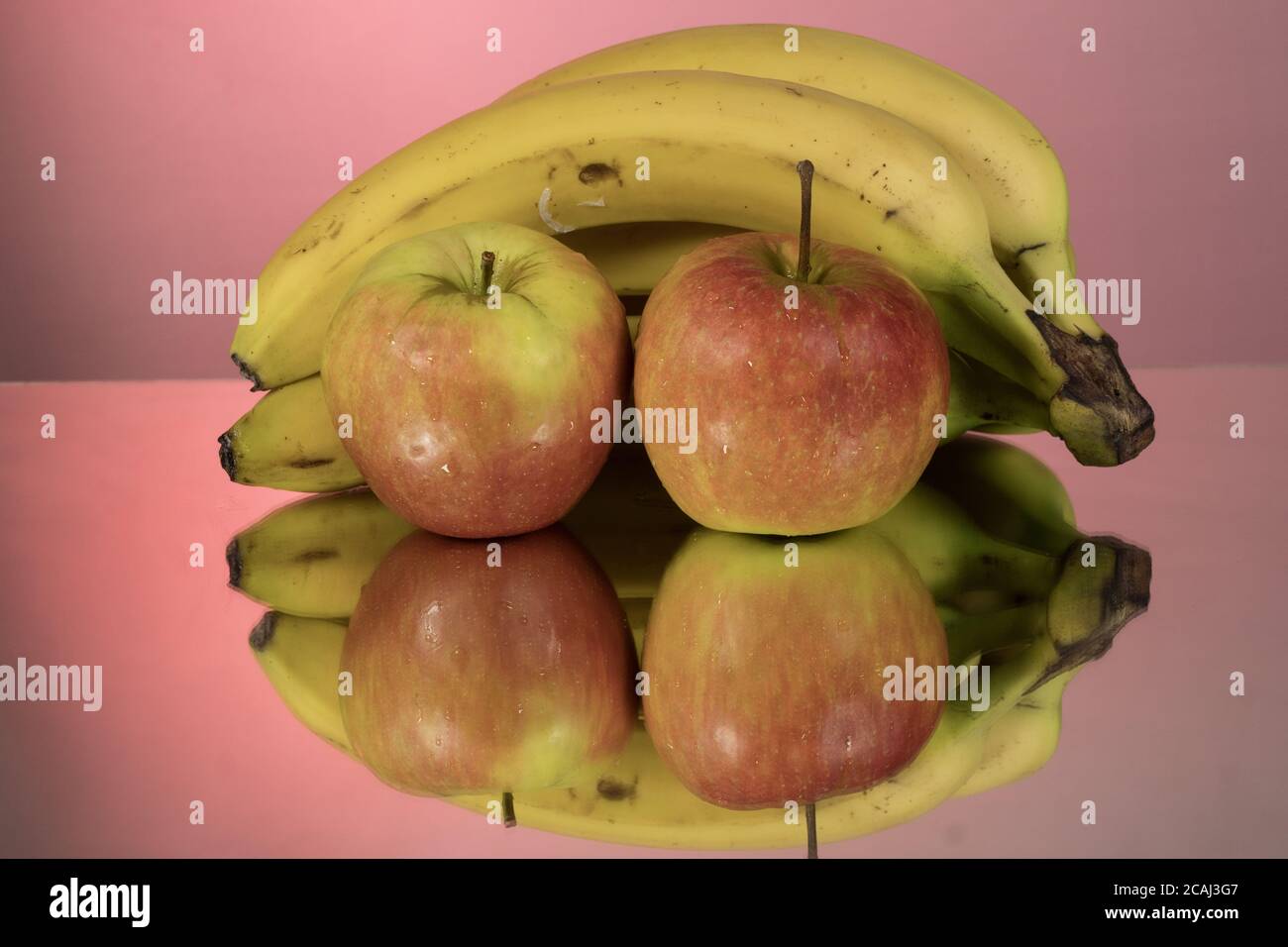 A bunch of bananas and apples on mirroring table on mirror red ...