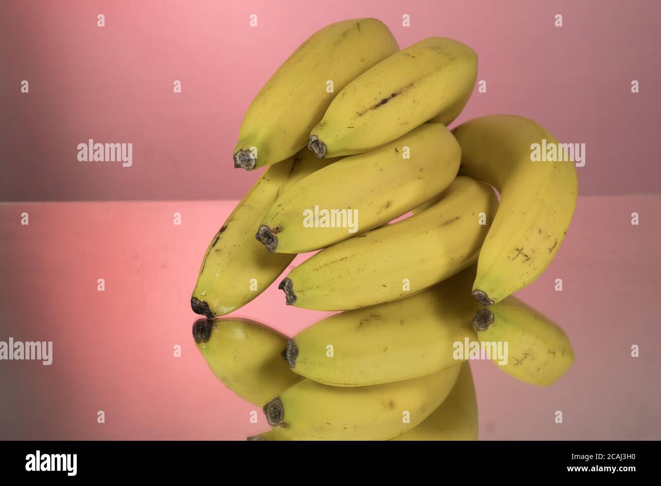 A bunch of bananas on mirroring table on mirror red background with ...