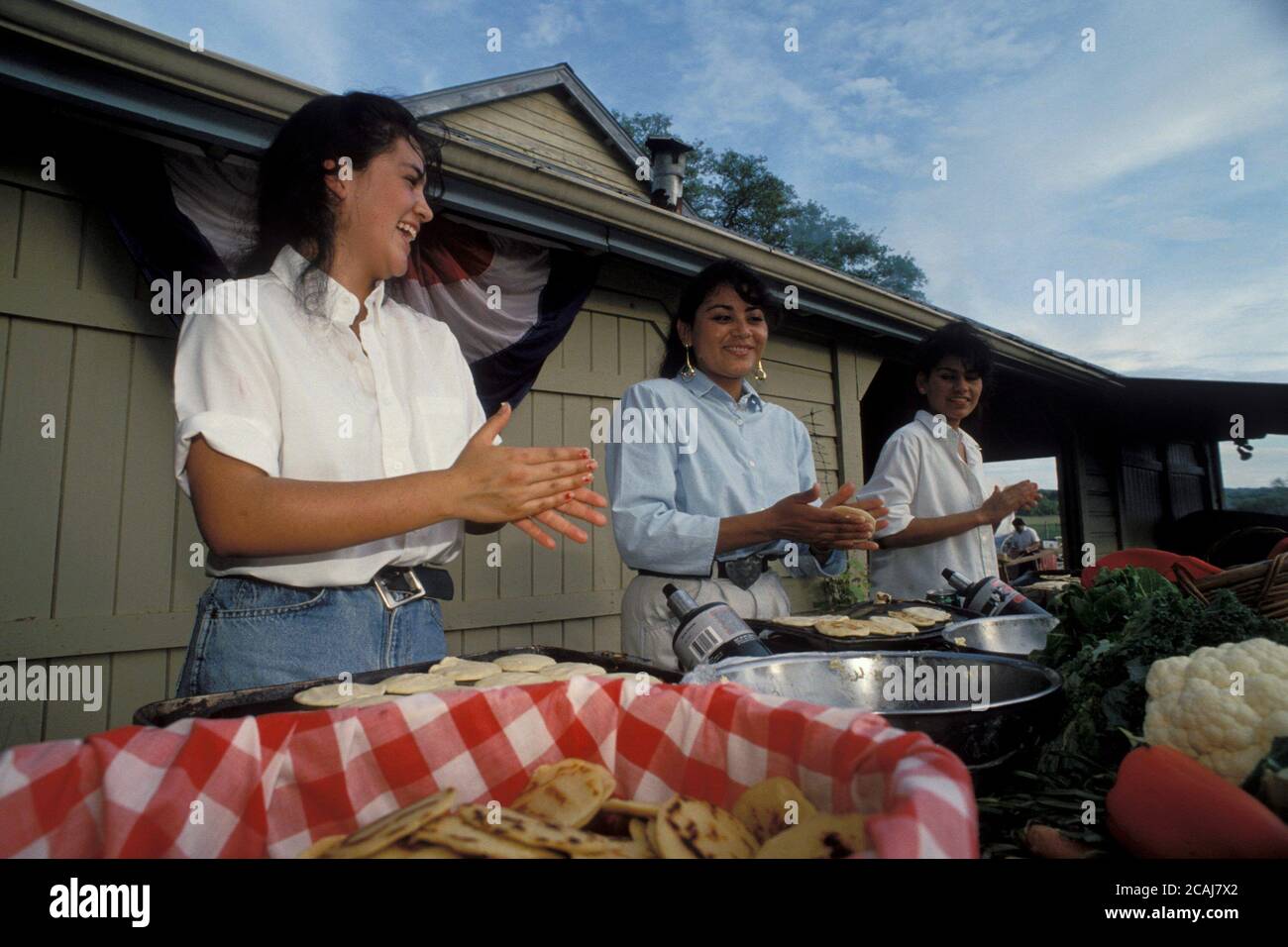 Three Hispanic women making gorditas at Mexican-style cookout at a ...
