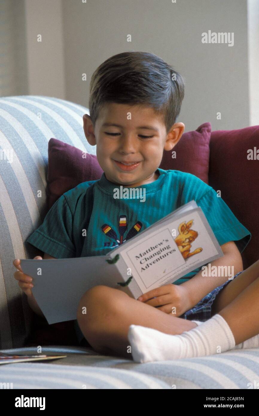 Young Hispanic boy reading large picture book on couch at home. Model ...