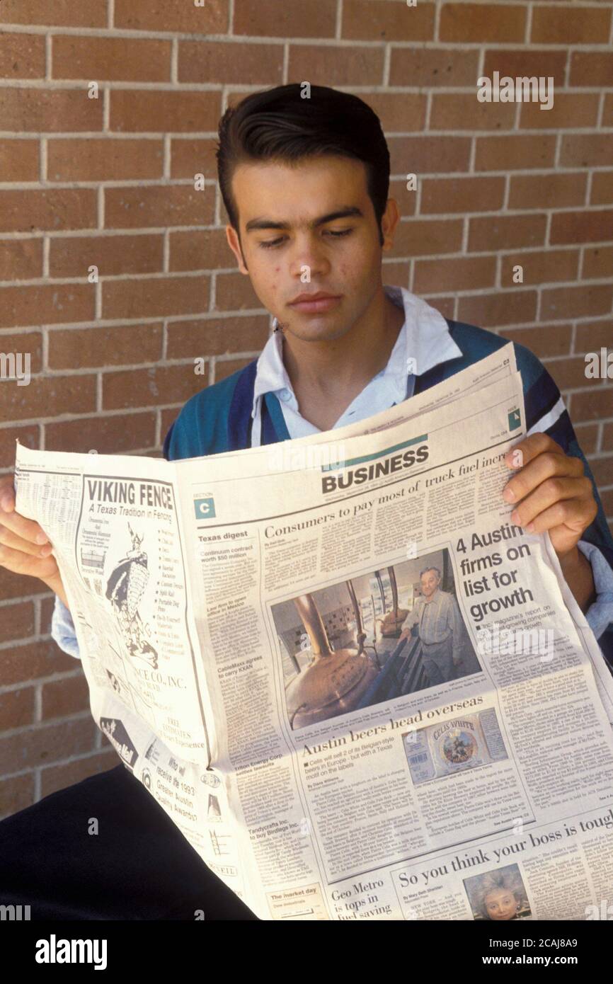 Male high school student reading business section of local newspaper in ...