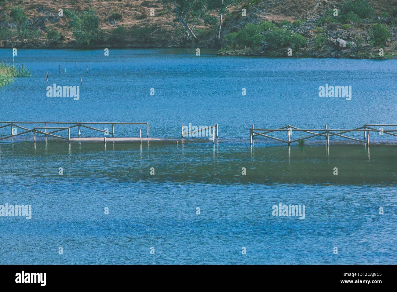 Old partially sunken wooden bridge over a tranquil lake surrounded by ...