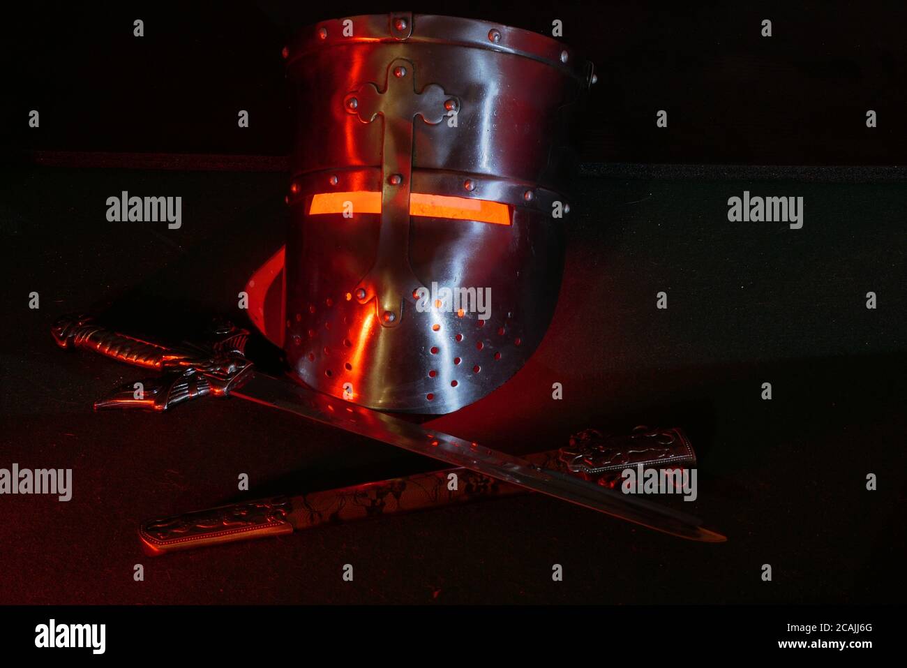 Medieval knight helmet illuminated with red light and with sword in the ...