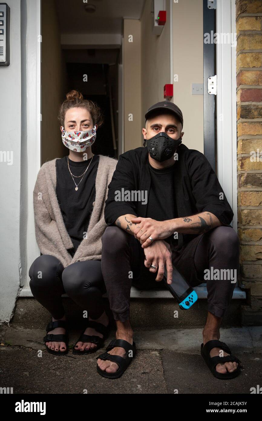 Two housemates wearing face masks sitting on the doorstep of their home ...