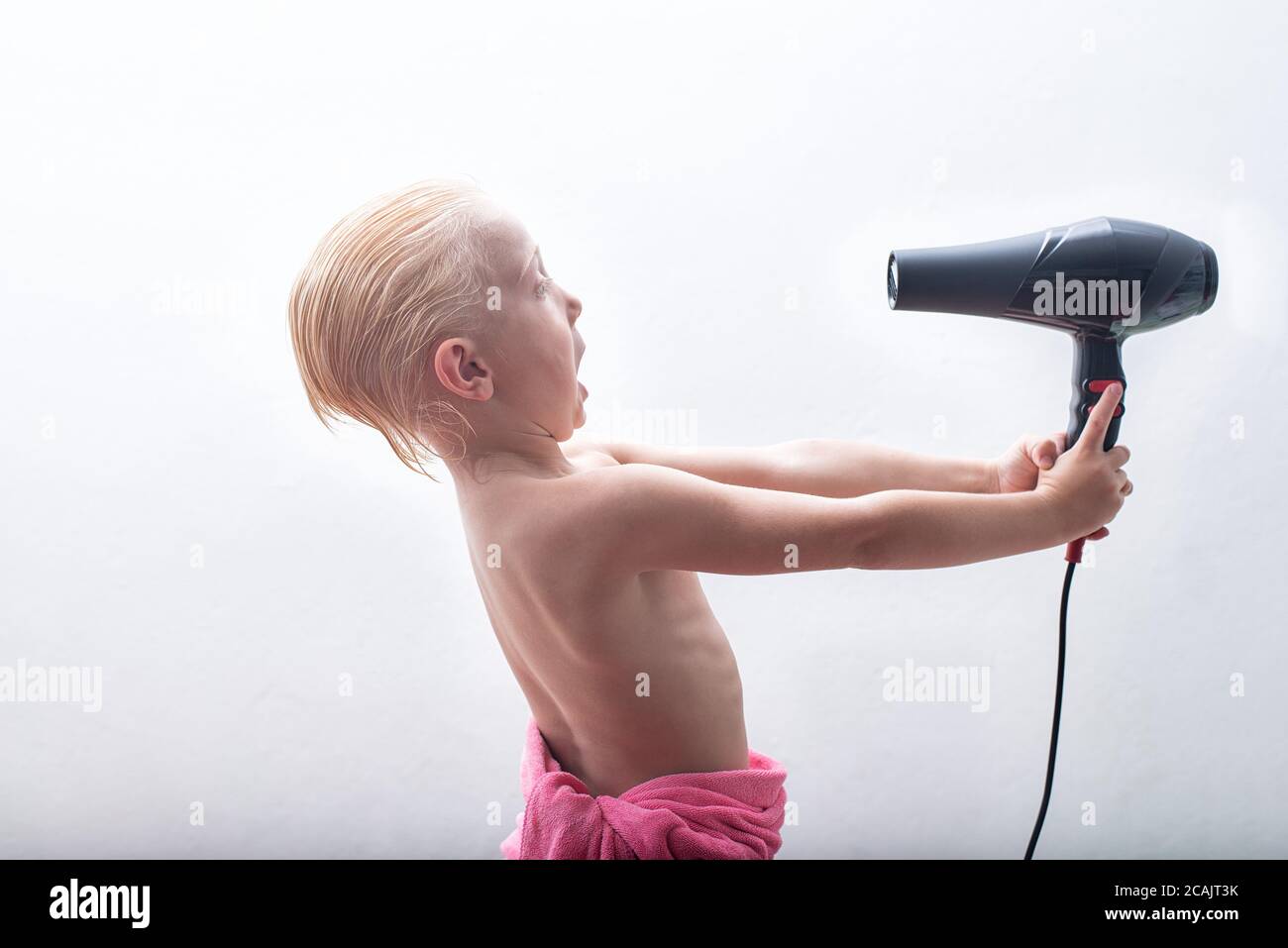 Blond boy with wet hair is funny dried by a hairdryer. White background ...