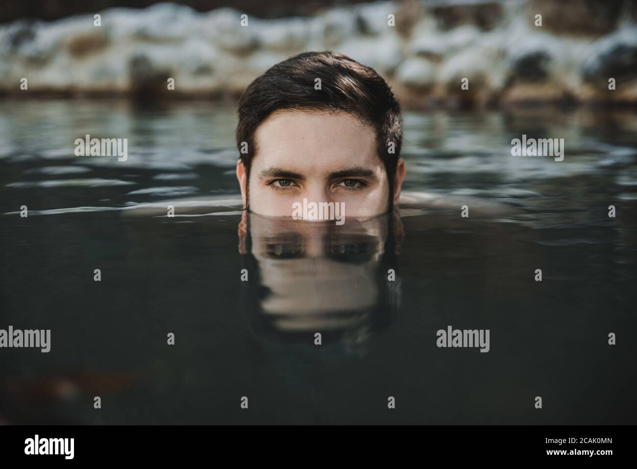 A horizontal shot of a man in a water pond with half of his face ...