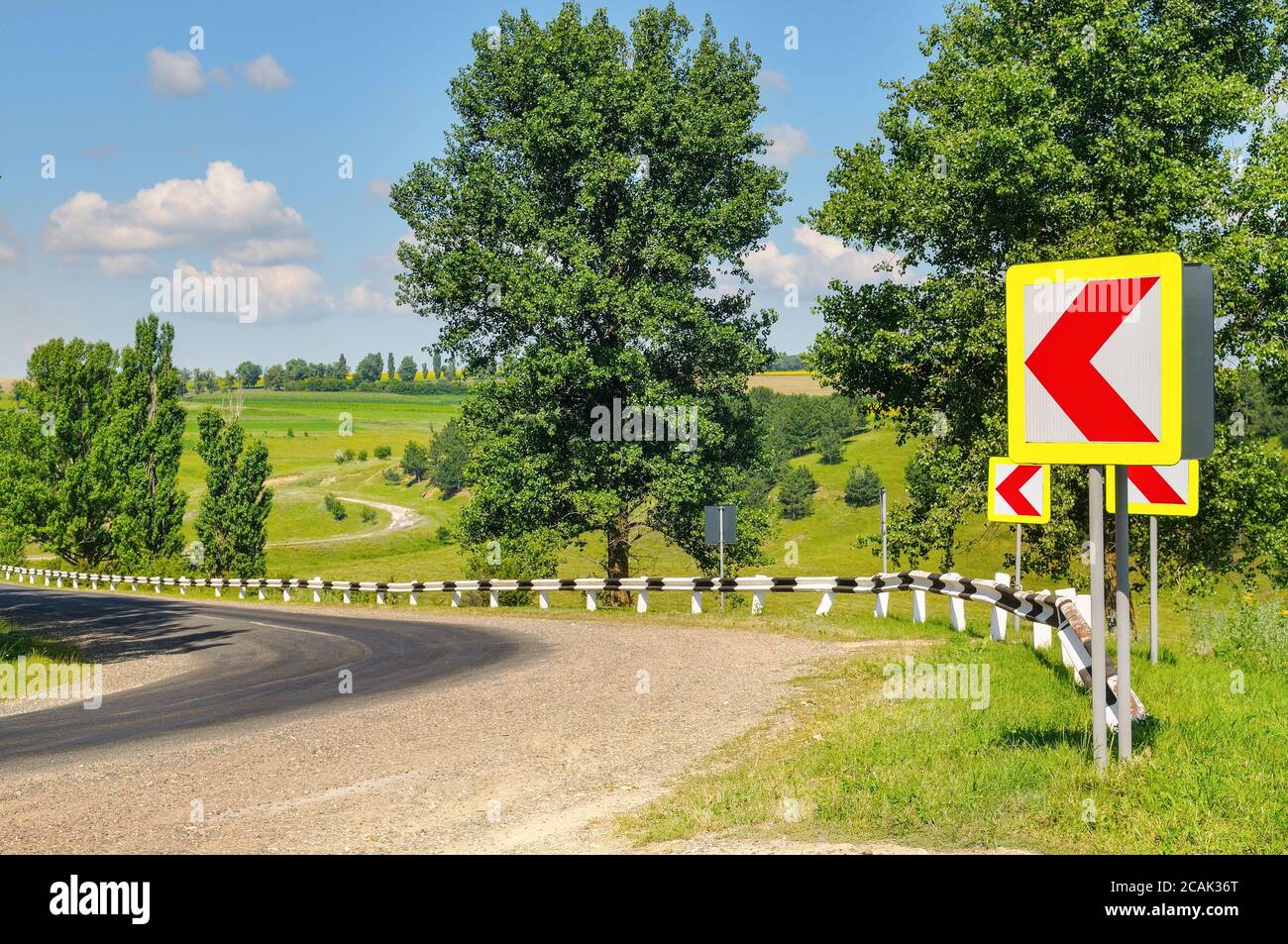 A winding road with steep turns in the hilly terrain. Warning signs ...