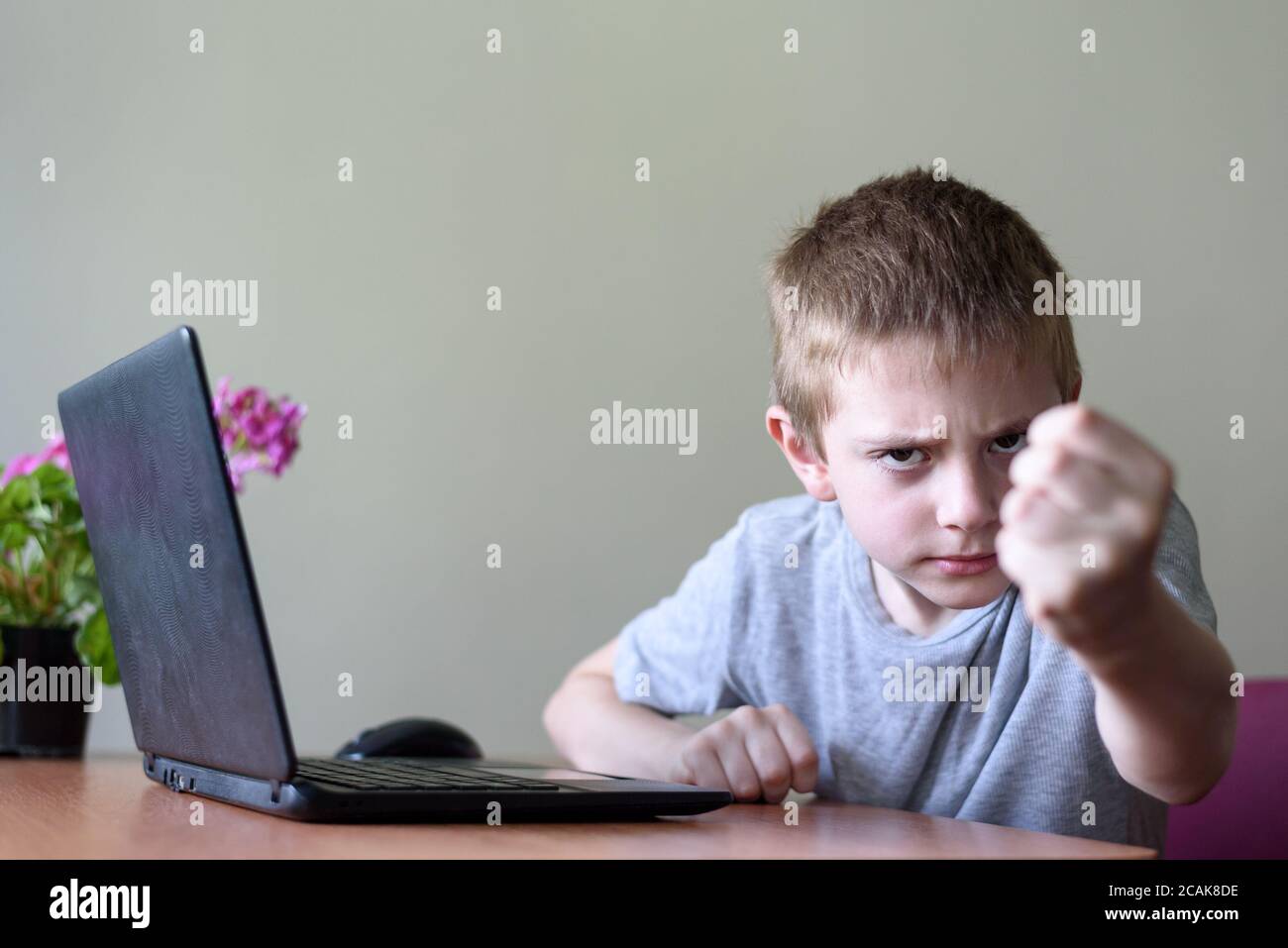 Angry boy sits at a laptop and shows a fist. Computer addiction Stock ...