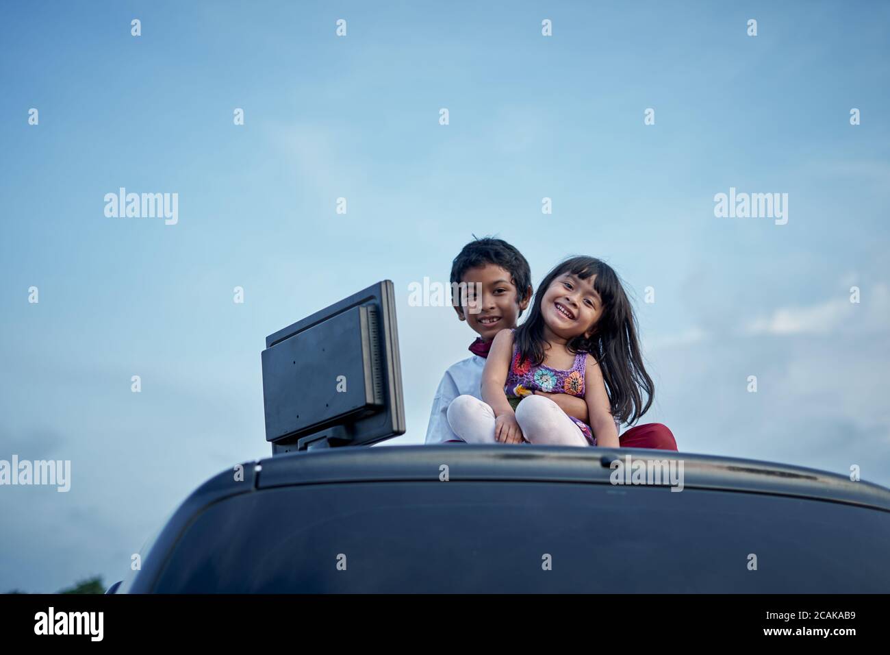 Boy and girl doing homework using computer on top of car roof, New ...