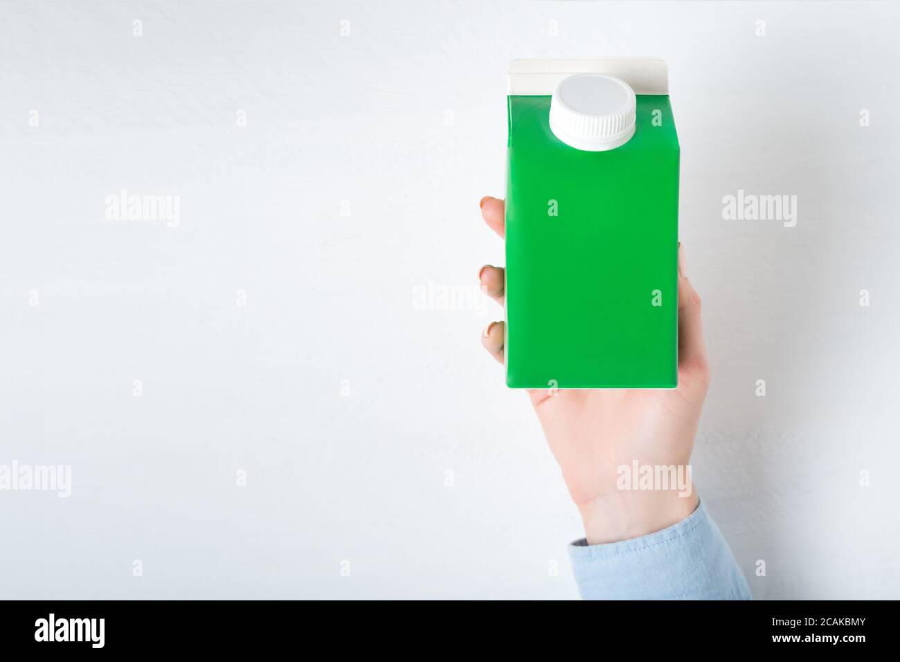 Green carton box or packaging of tetra pack with a cap in a female hand ...