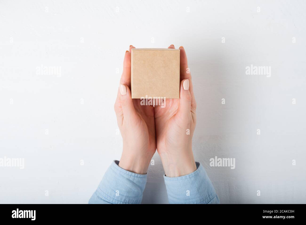 Small square cardboard box in female hands. Top view, white background ...