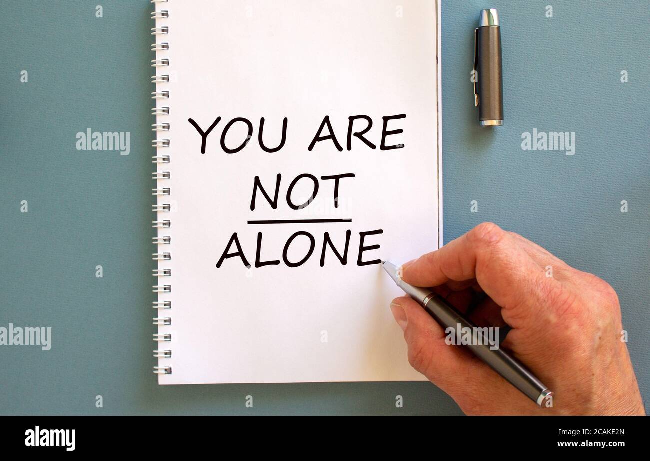 Male hand writing 'you are not alone' on white note, isolated on blue ...