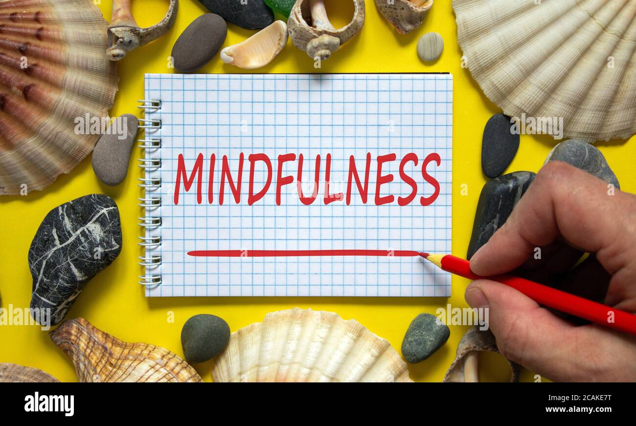 Male hand with red pencil writing 'mindfulness' on white note ...