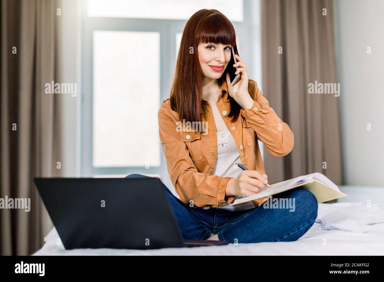 Smiling pleasant young Caucasian woman sitting on bed in lotus pose ...