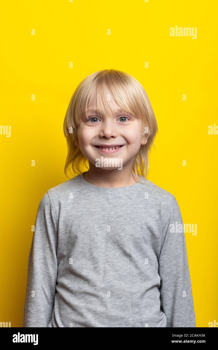 Portrait of cheerful fair-haired boy with long hair on bright yellow ...