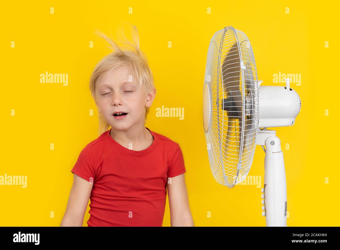 Fair-haired boy with fan relaxing on yellow background. Hot summer ...