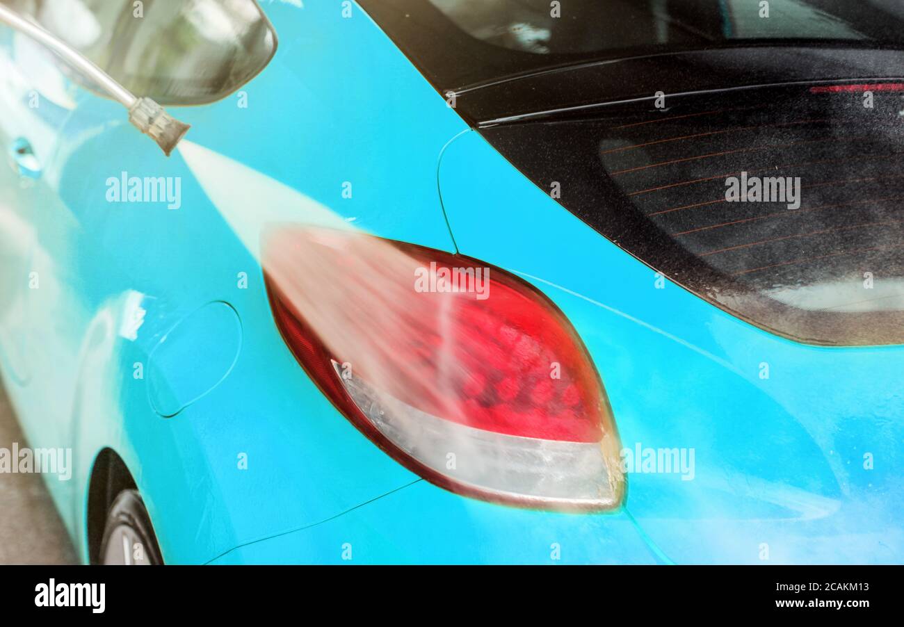 Rear light of blue car washed in self serve car wash, water spraying on ...