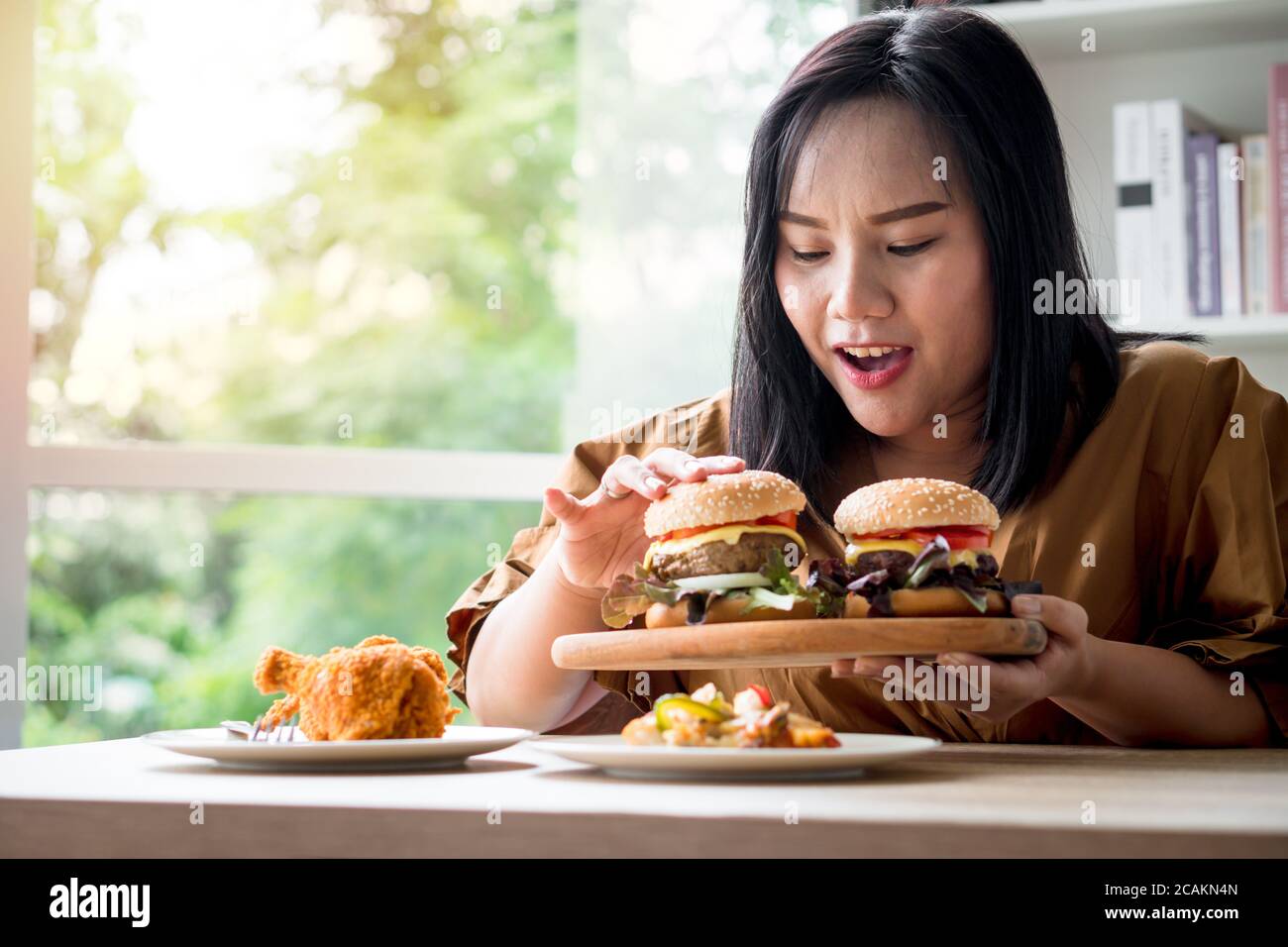 Hungry overweight woman holding hamburger on wooden plate after ...