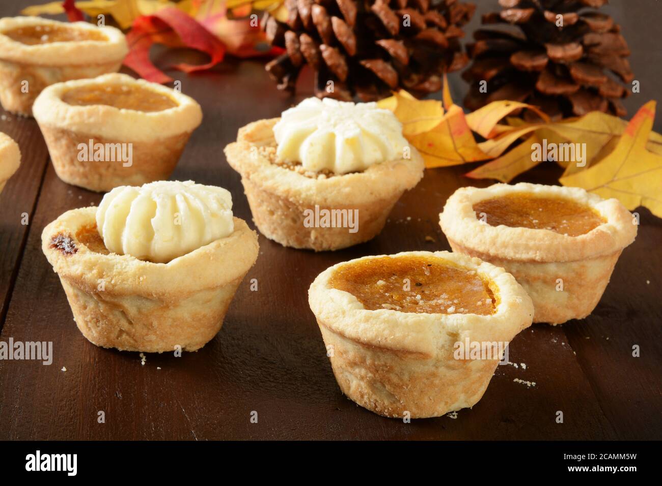 Assorted mini pumpkin tarts on a holiday table with pine cones and ...
