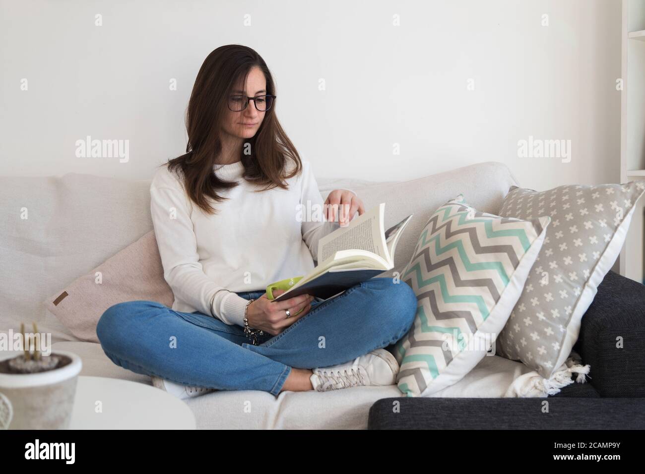 Young woman sitting on sofa and reading book. Woman alone at her home ...