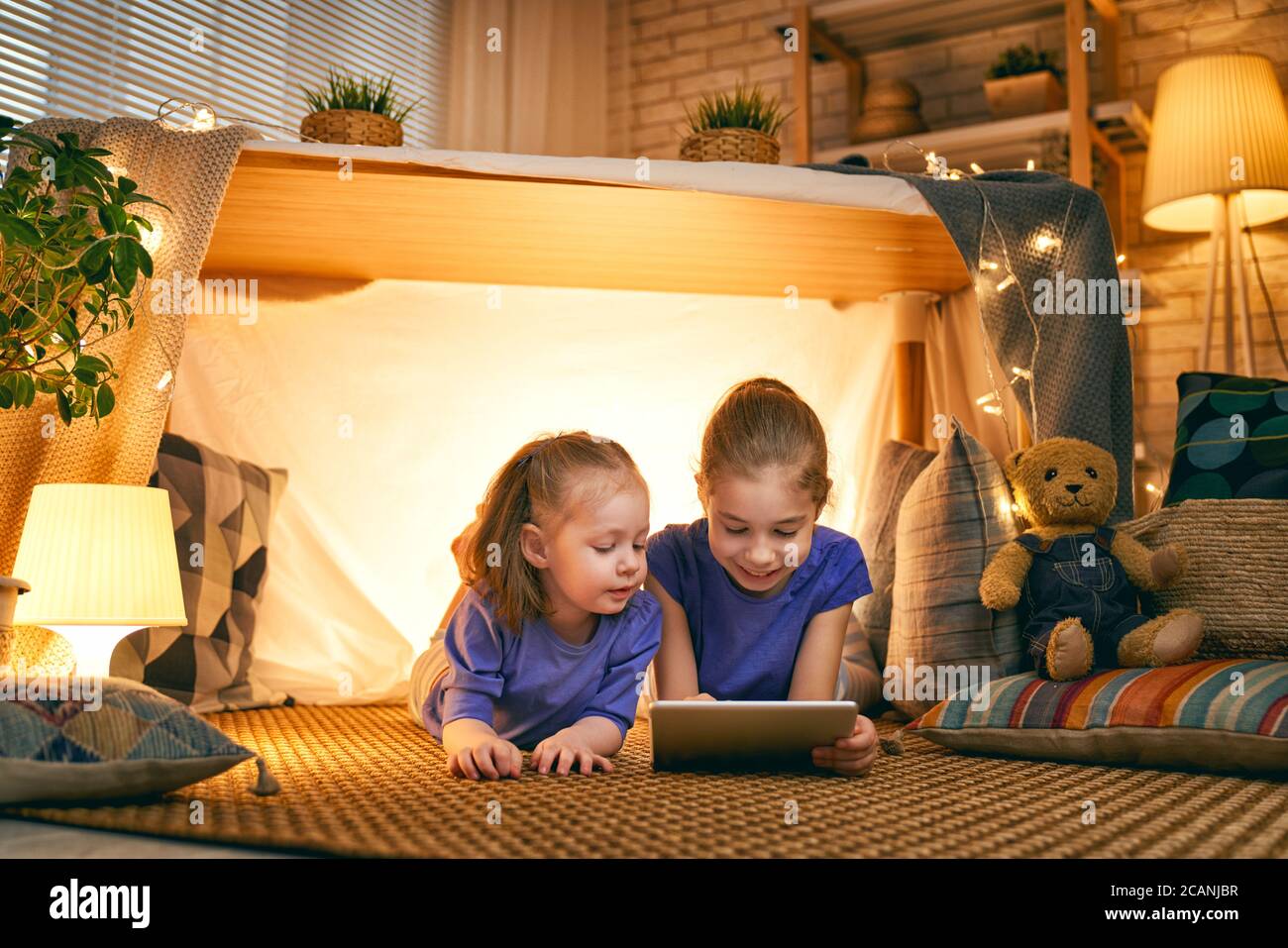 Cute little children are playing with tablet in tent. Happy girls at ...