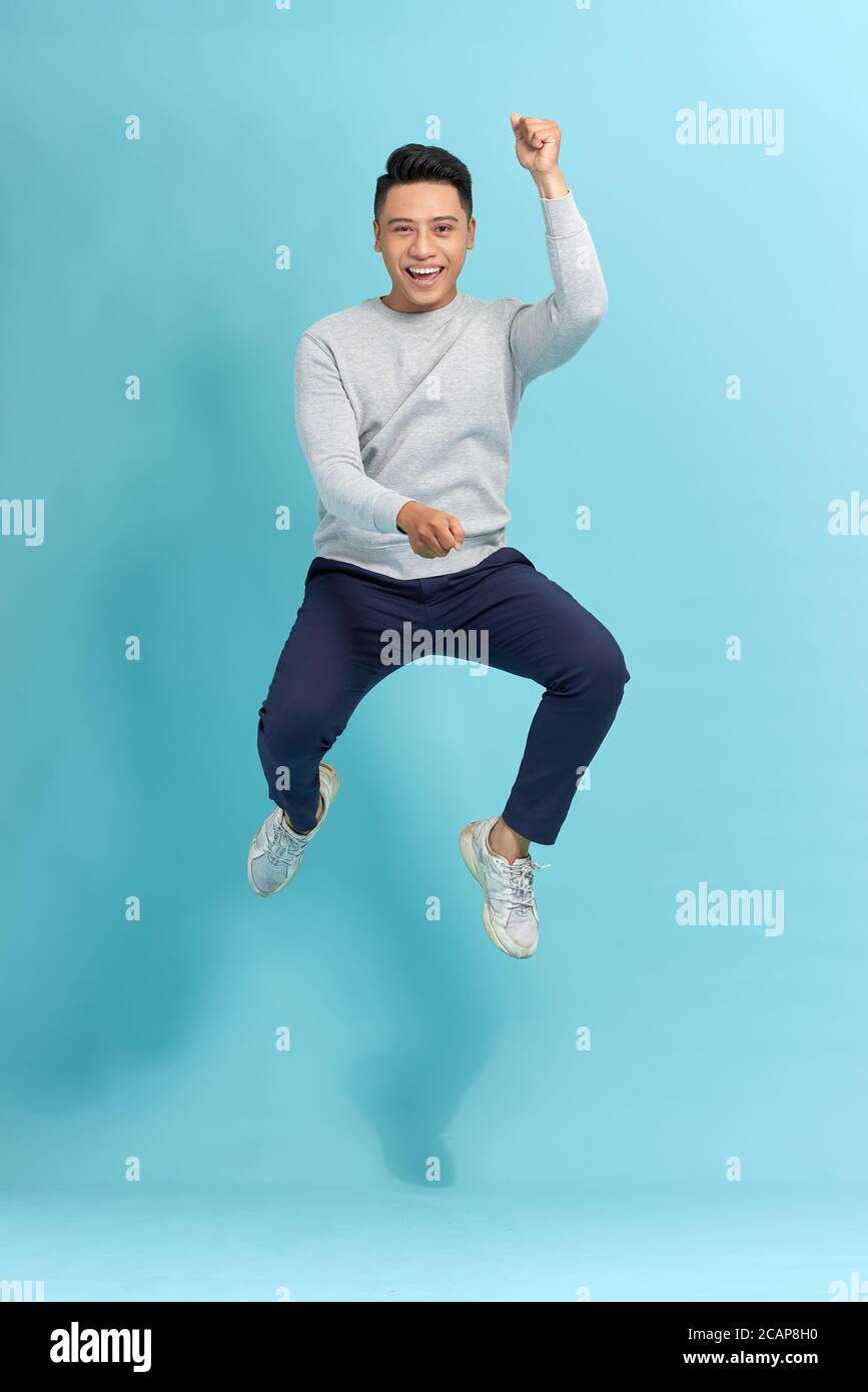 Vertical image of asian man jumping in studio. Isolated blue background ...